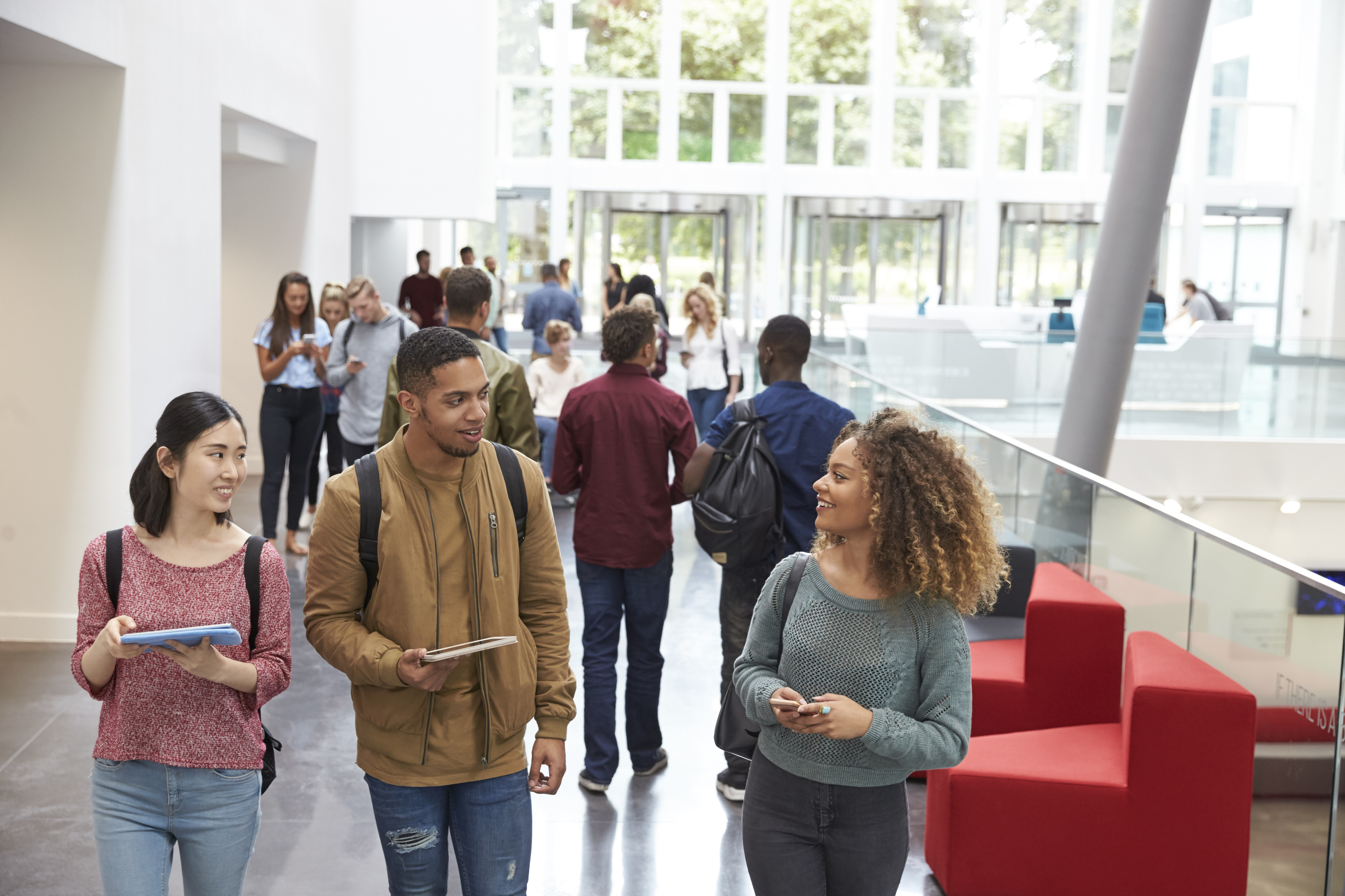 Students holding tablets and phone talk in university lobby - Great ...